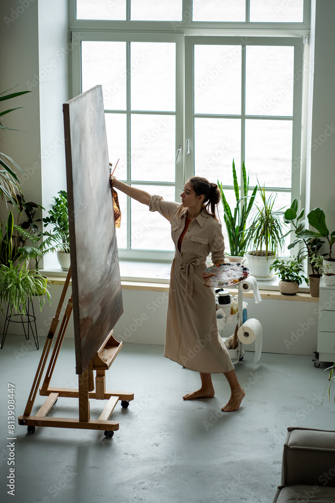 Creative female artist paints with oil on canvas, standing near easel ...