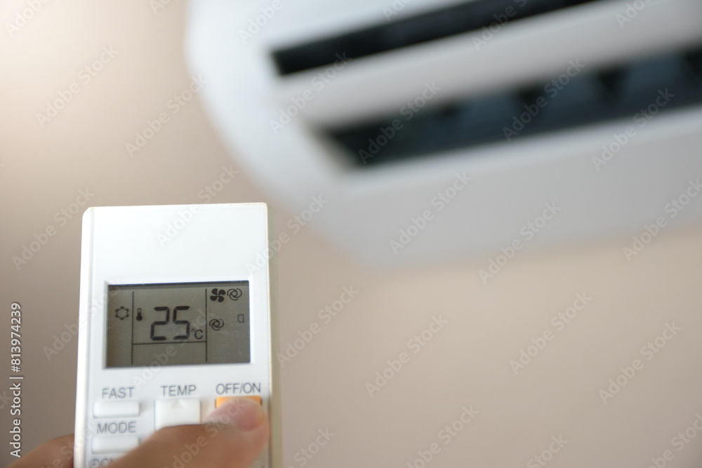 Hand holding remote control to turn on the air conditioner at 25 ...