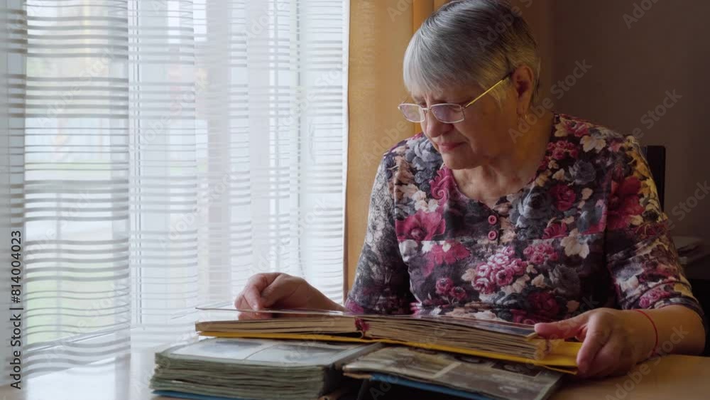 A 70-year-old elderly woman looks through photos from a family album ...