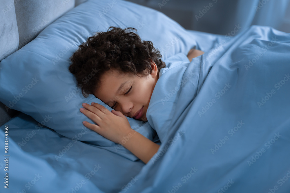 African American young boy is peacefully sleeping in a bed with blue ...