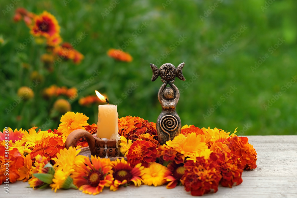 Triple Goddess figurine with candle and colorful flowers in garden ...