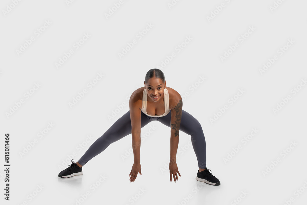 African American woman is seen performing a squat exercise on a white ...