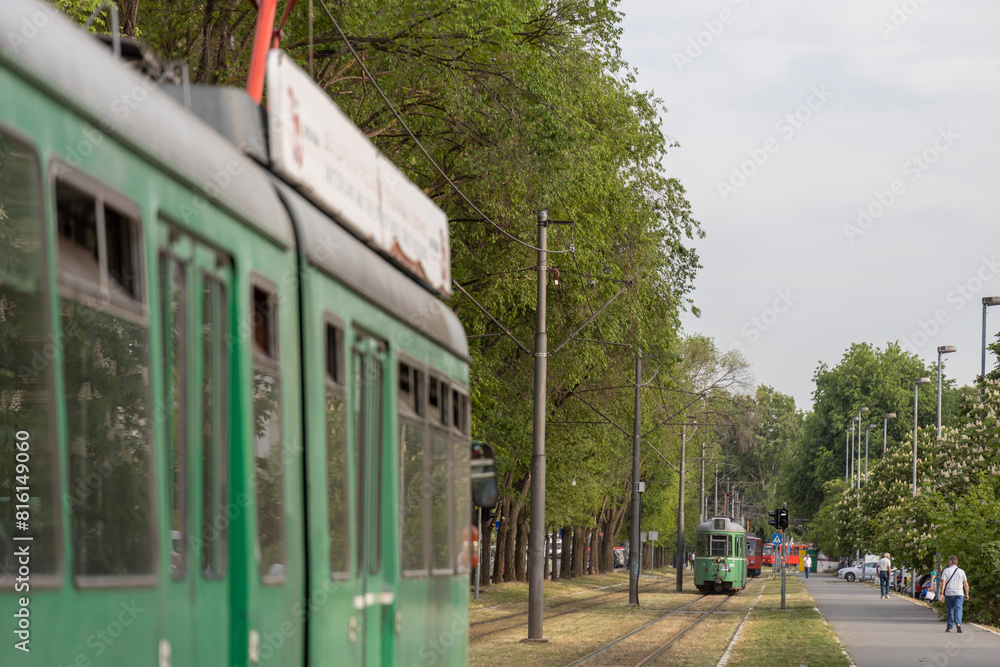 A daytime city street scene featuring a green tram in motion, with ...