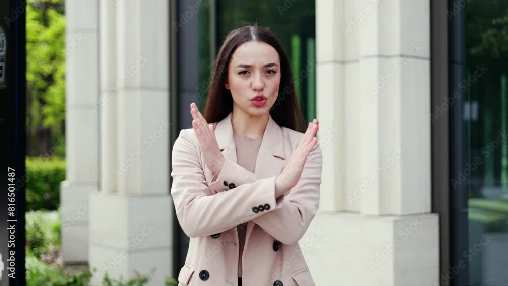 Serious caucasian female in stylish jacket raising hands in cross sign ...