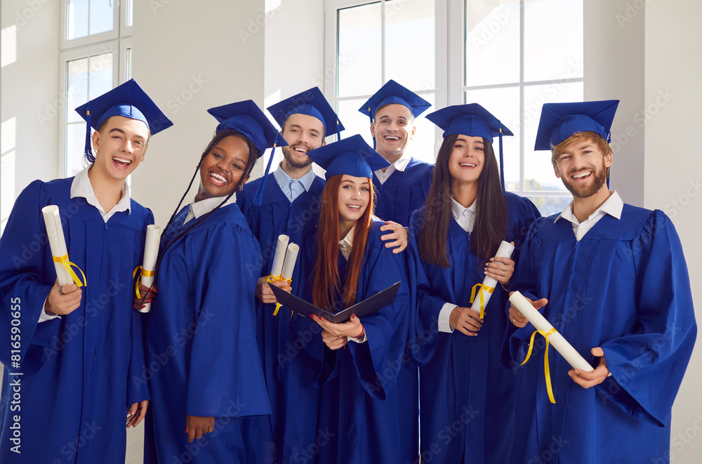 Diverse group of a young joyful people wearing blue graduation gowns ...