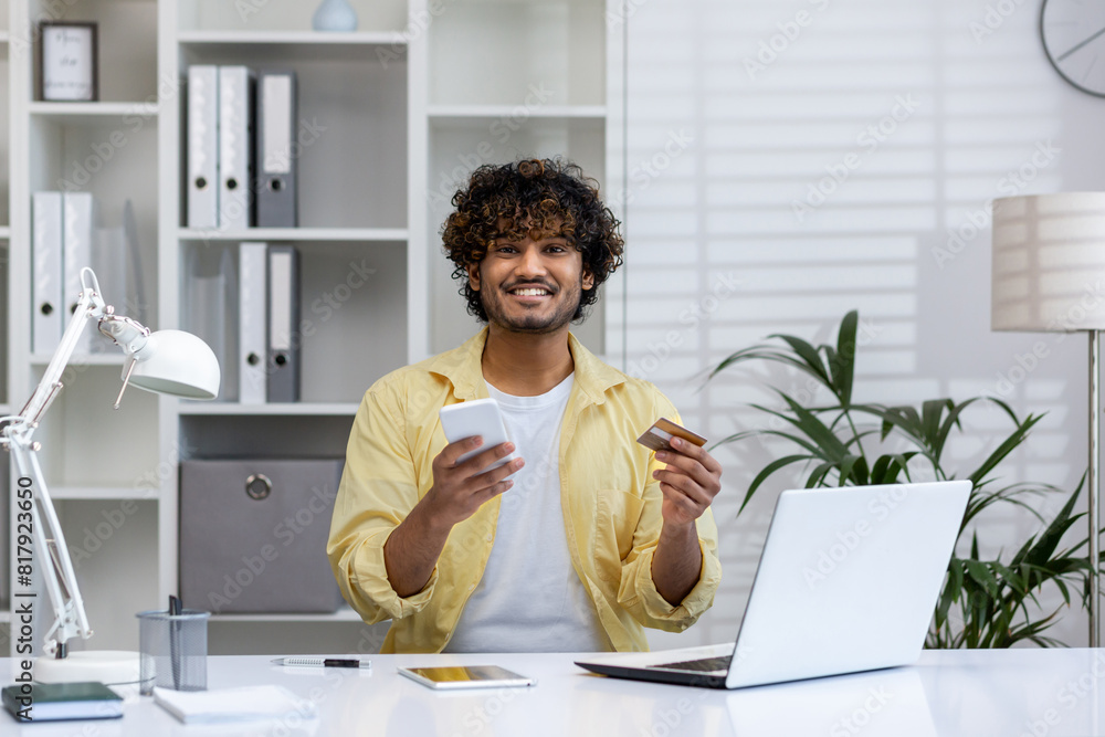 Smiling man using smartphone and credit card for online shopping at a ...