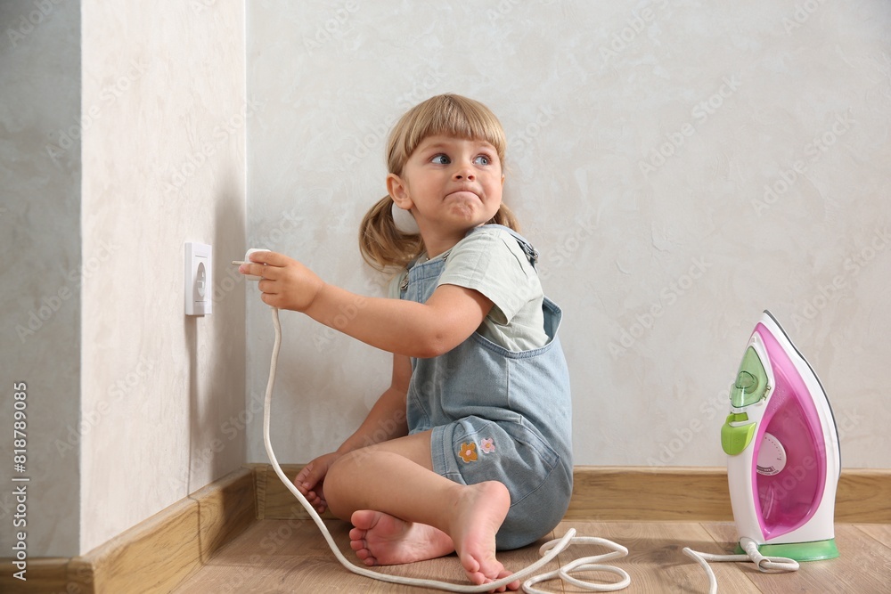 Little child playing with electrical socket and iron plug at home ...