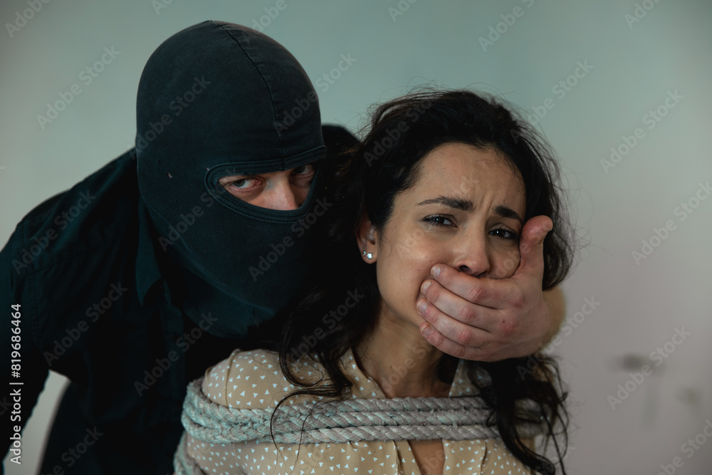Male kidnapper in a black balaclava covering mouth of frightened woman ...