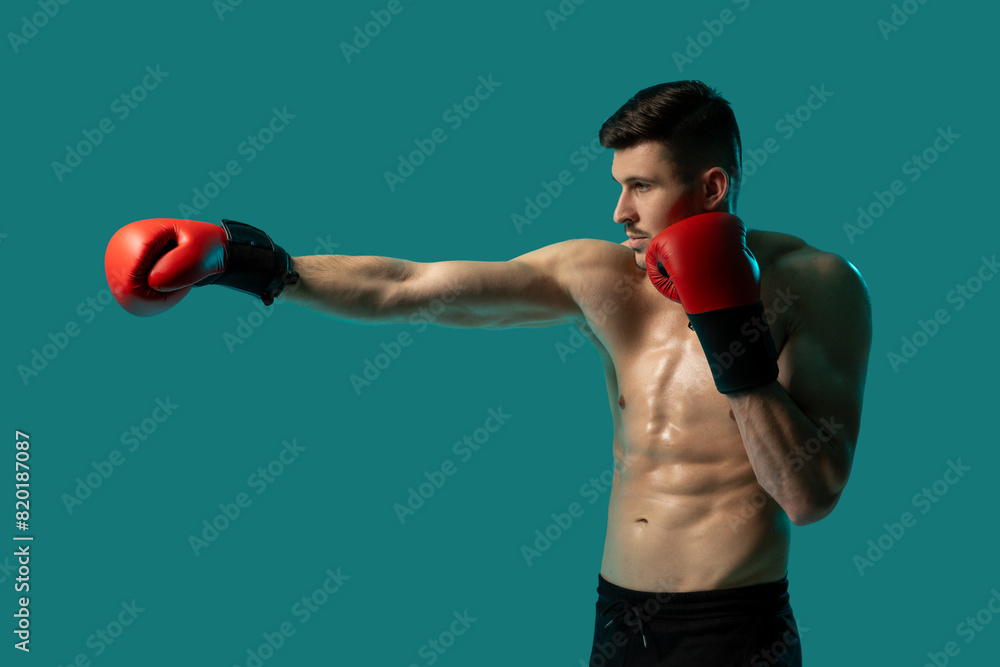 A muscular man is practicing boxing by throwing punches indoors against ...