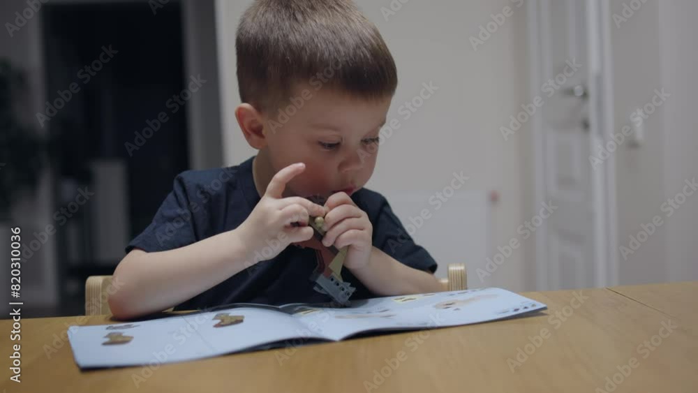 Sitting at table young child playing toy constructor following ...