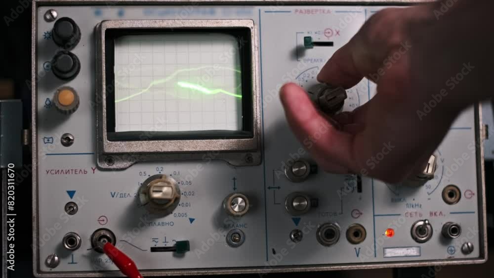 Zoom in on a hand adjusting knobs on a vintage oscilloscope ...