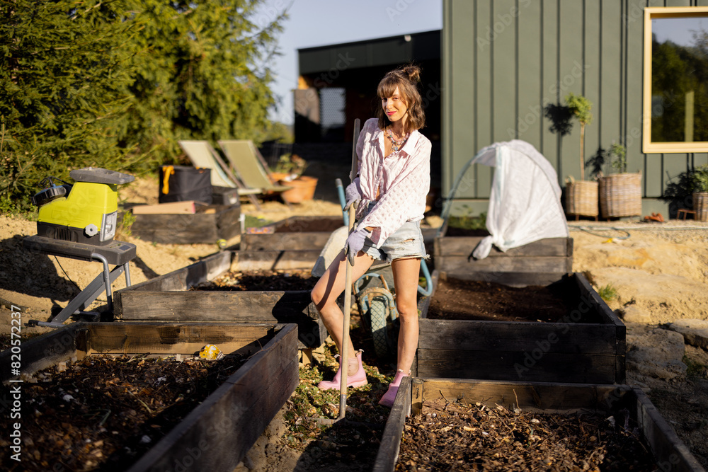 Portrait of a young woman works on her backyard garden, mulching with ...