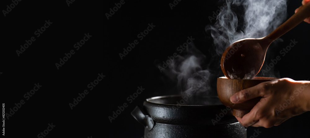 The cook is cooking rice porridge in a boiling clay pot with steam ...