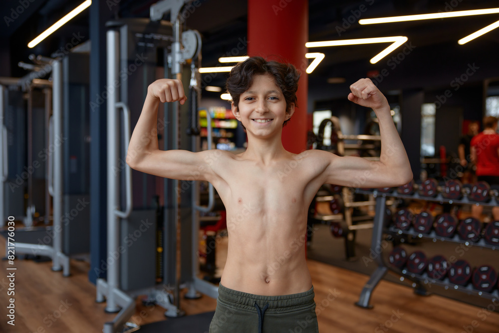 Skinny preteen boy demonstrating pumped arm muscles after gym training ...