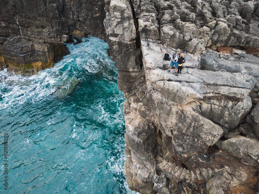 A couple stands on a steep shore near the ocean. Boca do Inferno (Devil ...