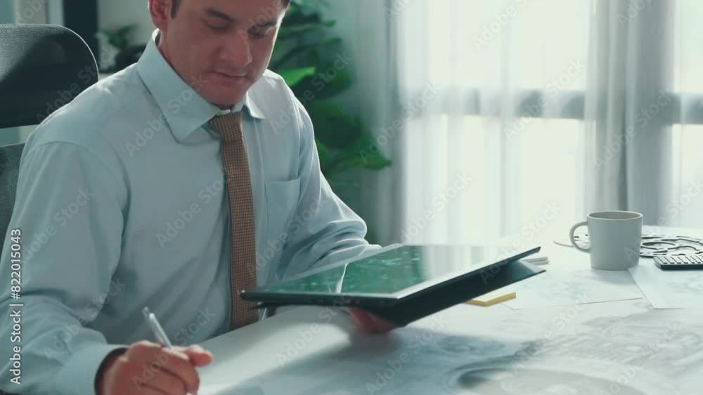 Professional engineer looking at phone while working on tablet with ...