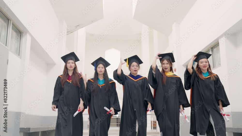 A group of five women in graduation gowns walk down a hallway. Scene is ...