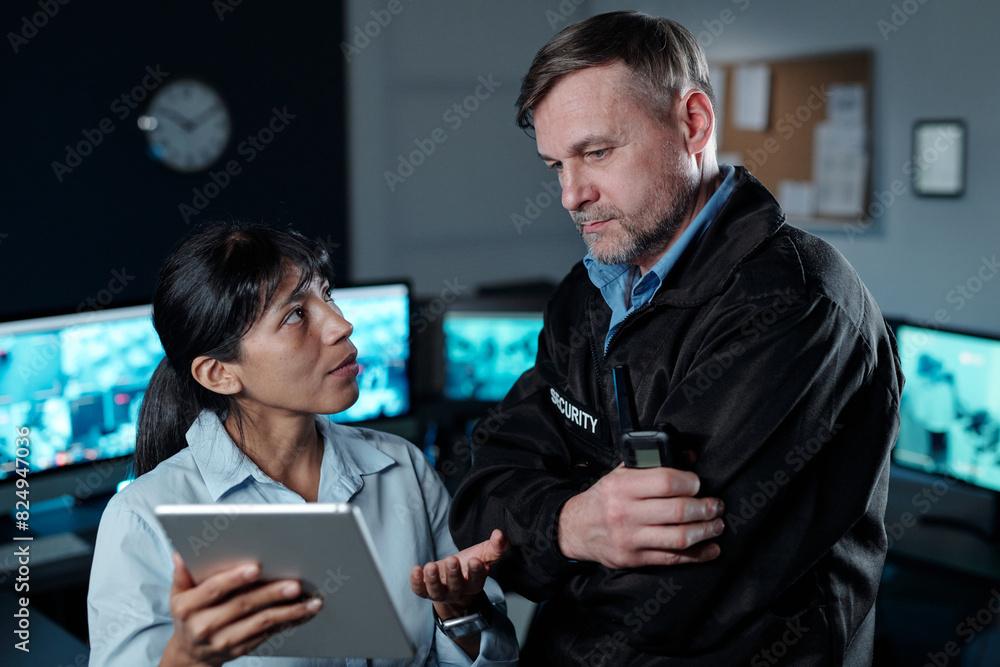 Young Hispanic female security guard with tablet looking at mature male ...