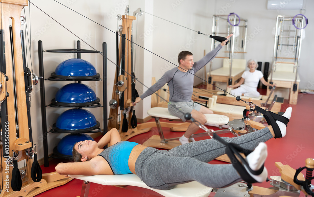 Girl in prone position is engaged in Pilates simulator with cable and ...