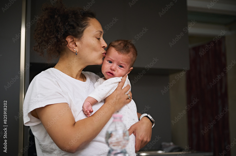 Affectionate young mother kissing temple of her child's head, measuring ...