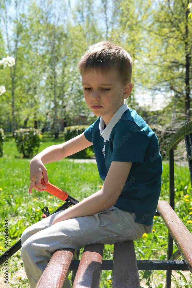 Boy is crying alone in park on bench, sitting and sad because of broken scooter. Child broke toy ...