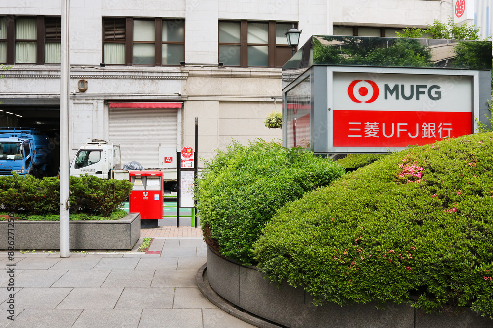 TOKYO, JAPAN - May 23, 2024: A sign outside MUFG bank's Nihonbashi branch. There is a post box ...