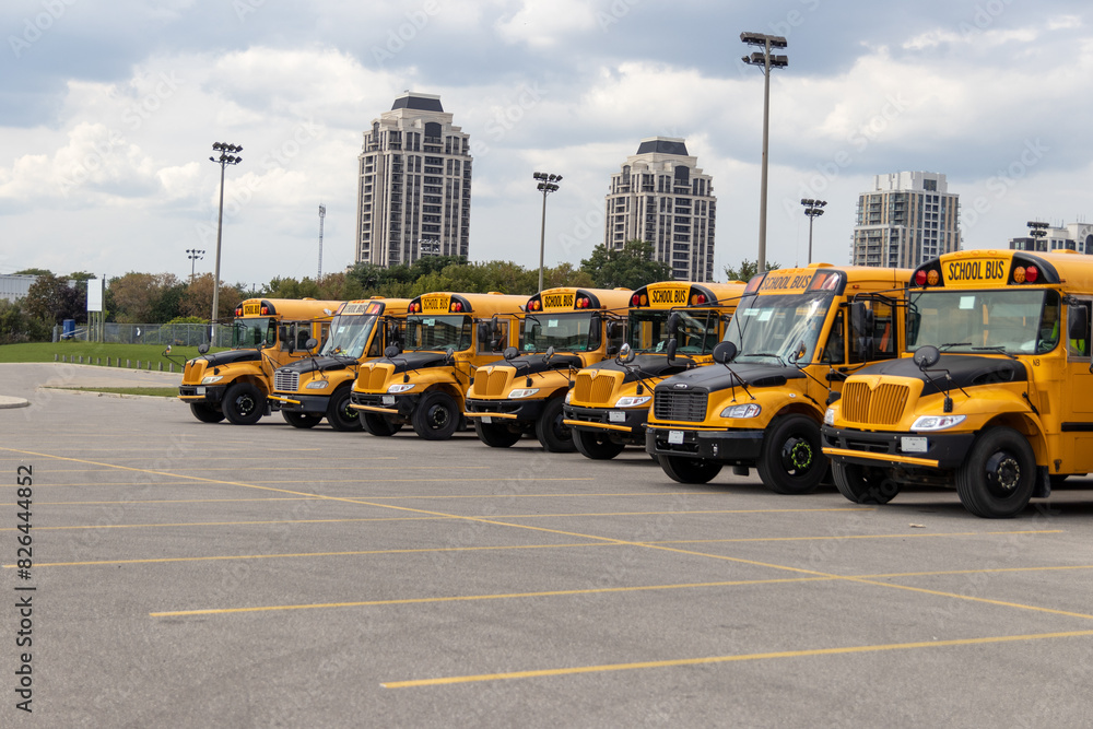 Yellow school buses lined up in empty parking lot - modern buildings ...