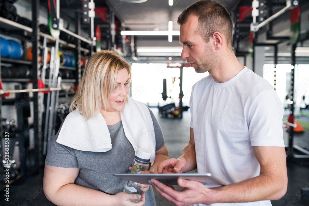 Overweight woman consulting with trainer, discussing daily workout plan ...