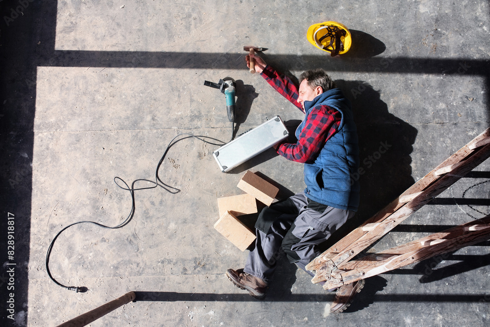 Male worker lying on the floor after fall from ladder, holding his knee ...