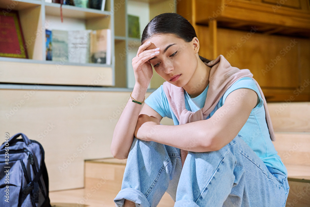 Upset sad teenage girl high school student sitting on floor in library ...