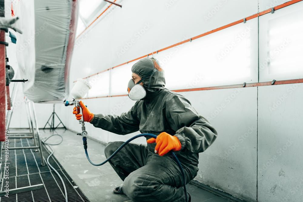 Auto painter painting a car with vaporizer gun inside a paint booth ...