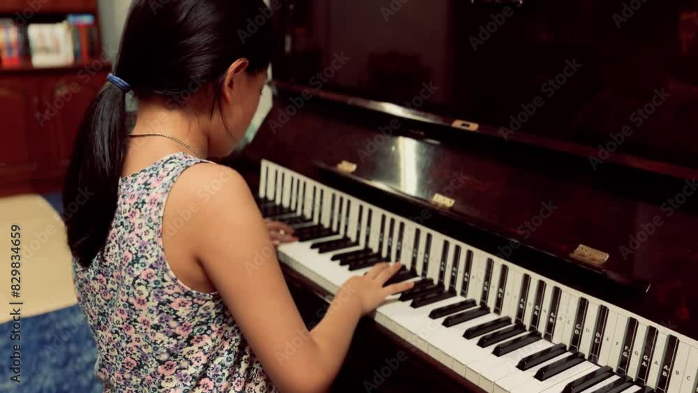 Behind the little Asian girl playing upright piano at home, using a ...