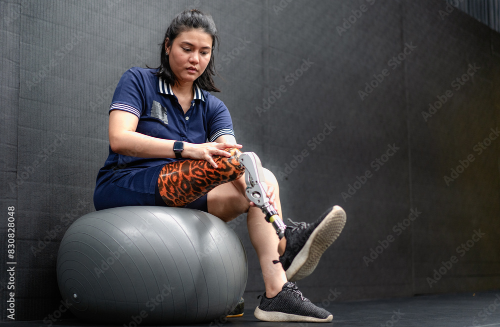 Woman with prosthetic leg sits isolated in gym. Asian female with foot ...