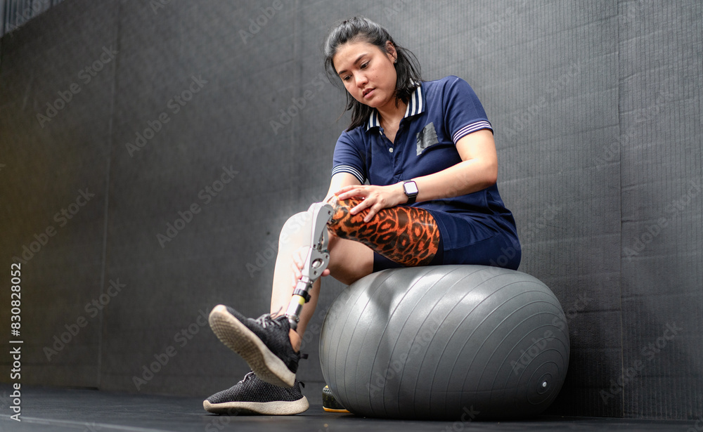Woman with prosthetic leg sits isolated in gym. Asian female with foot ...