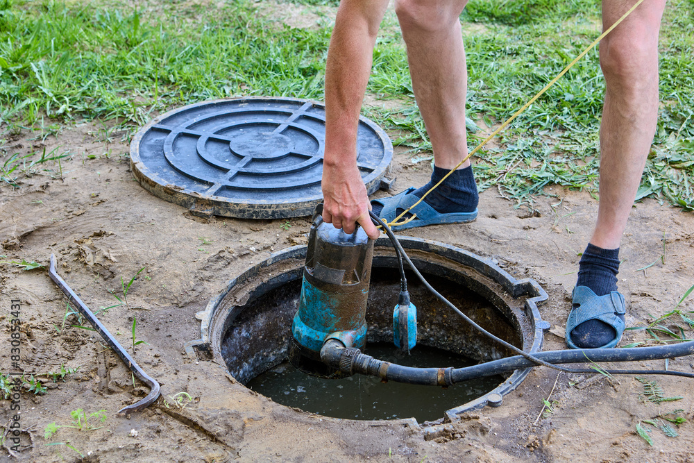 Worker pumps sewage out of septic tank using submersible drainwater ...