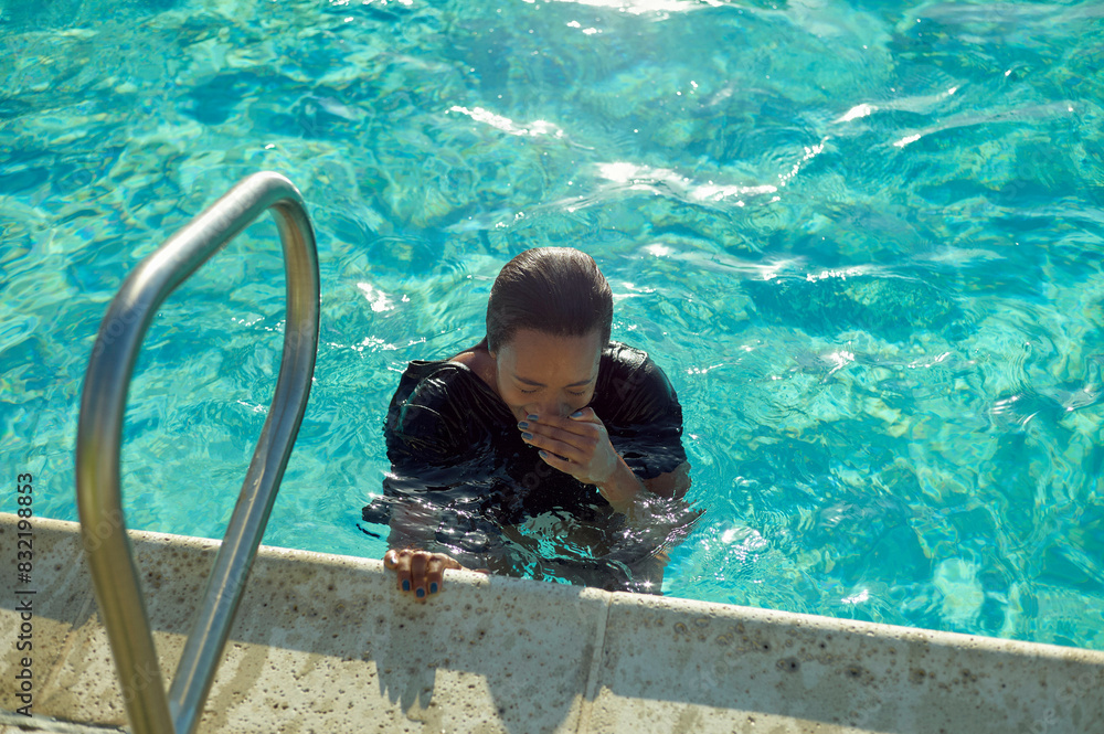 A person with wet hair is immersed in a swimming pool, holding onto the ...