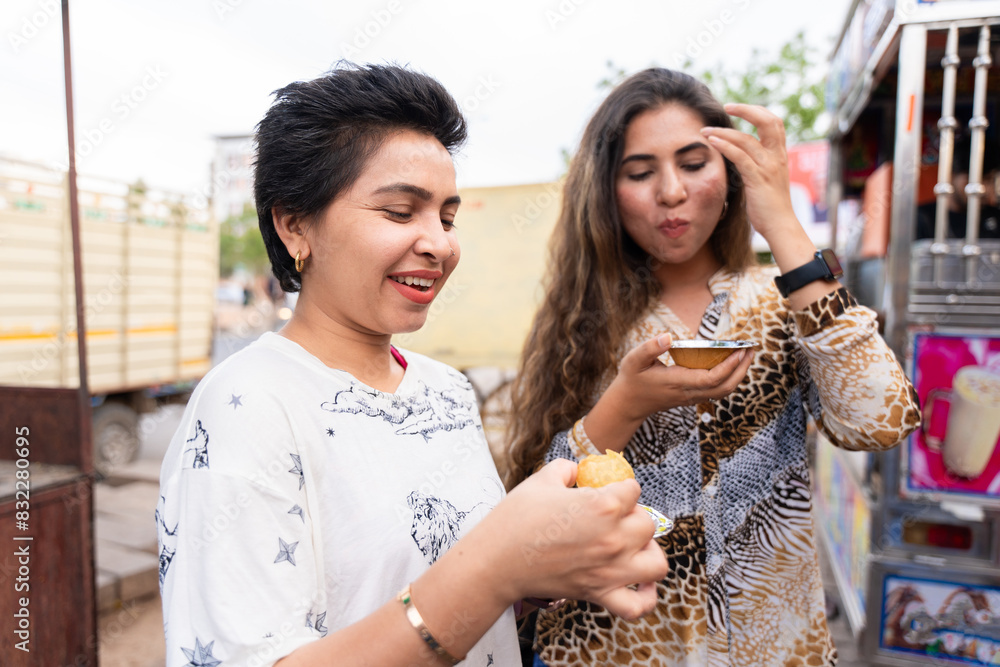 Two Cheerful indian girls eating Pani puri, golgappa on roadside. Two ...