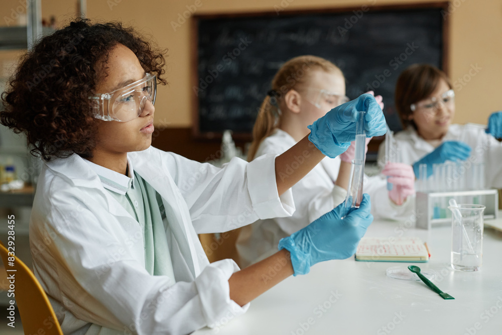 African American schoolboy wearing lab coat sitting at table in ...