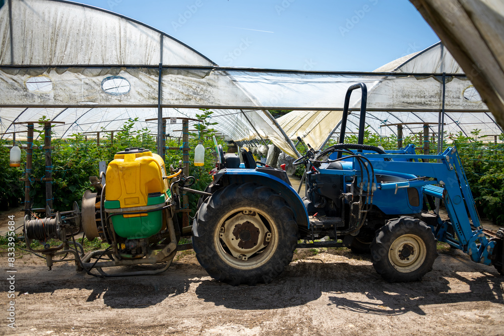 Blue tractor fitted with a yellow and green sprayer, parked outside a ...