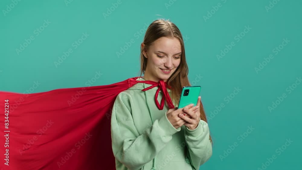 Young girl wearing superhero costume texting friends using smartphone, studio backdrop. Woman ...