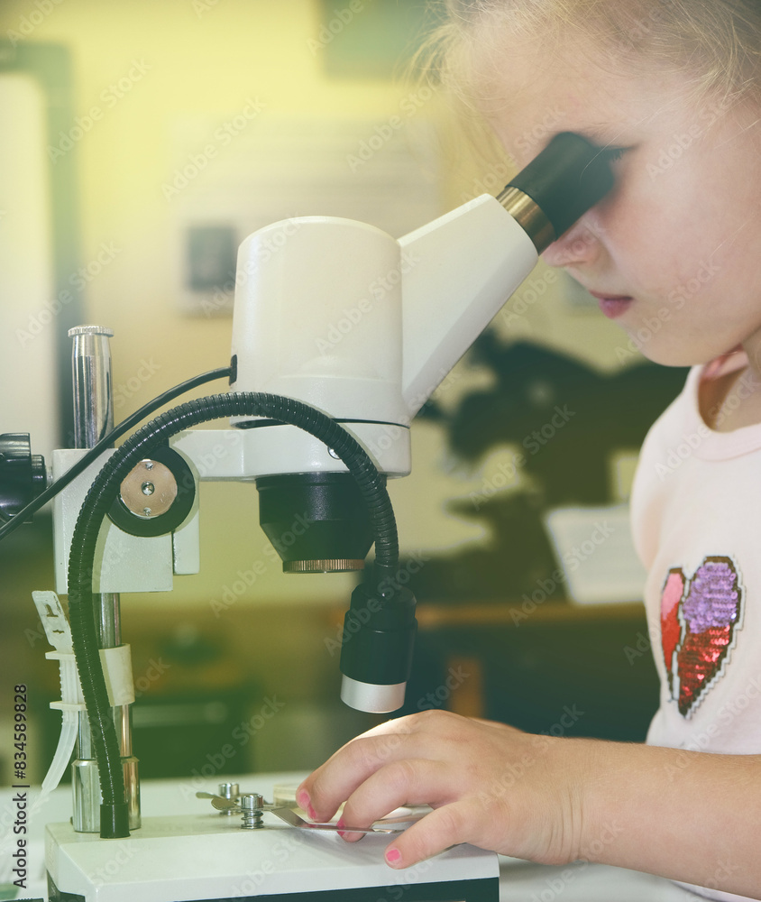 Little girl conducts experiment with microscope, looks through a ...