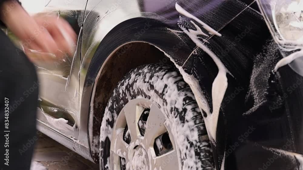 Close-up of a man's hand washing a car's alloy wheels with a sponge and ...