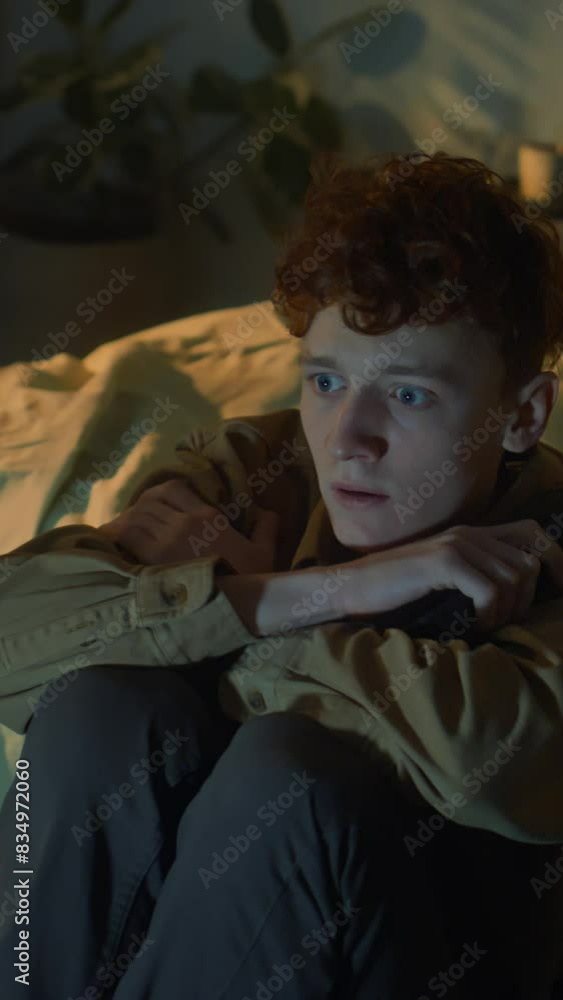 Vertical handheld footage of gen Z guy sitting on floor in front of TV ...