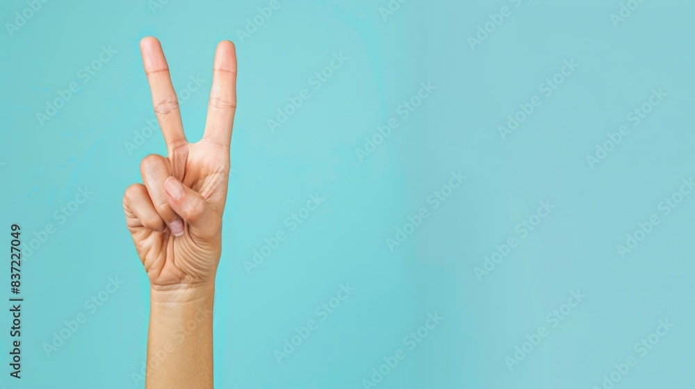 Hand showing two fingers in peace sign on light blue background Stock ...