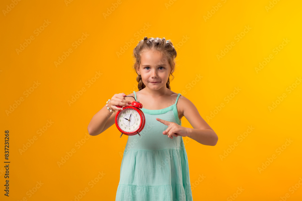 Smiling kid girl holding an alarm clock in hand and pointing finger at ...