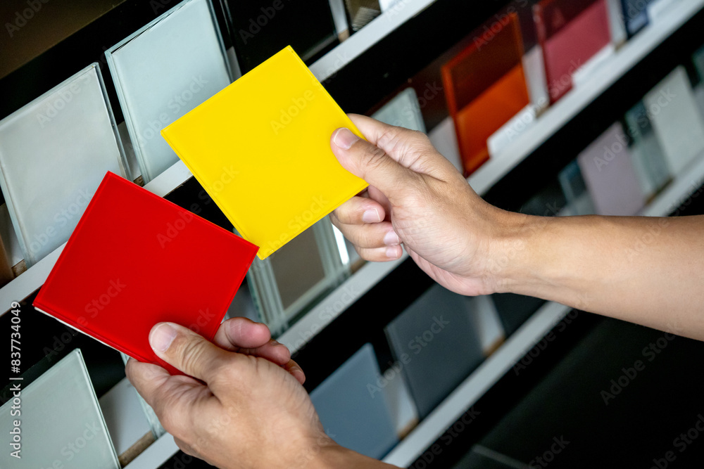 Designer hand compares yellow and red lacquered glass tiles from ...