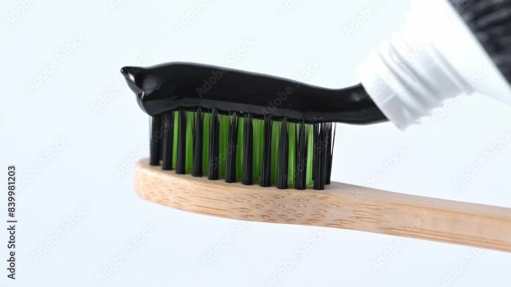 Putting charcoal toothpaste on bamboo toothbrush on white background ...