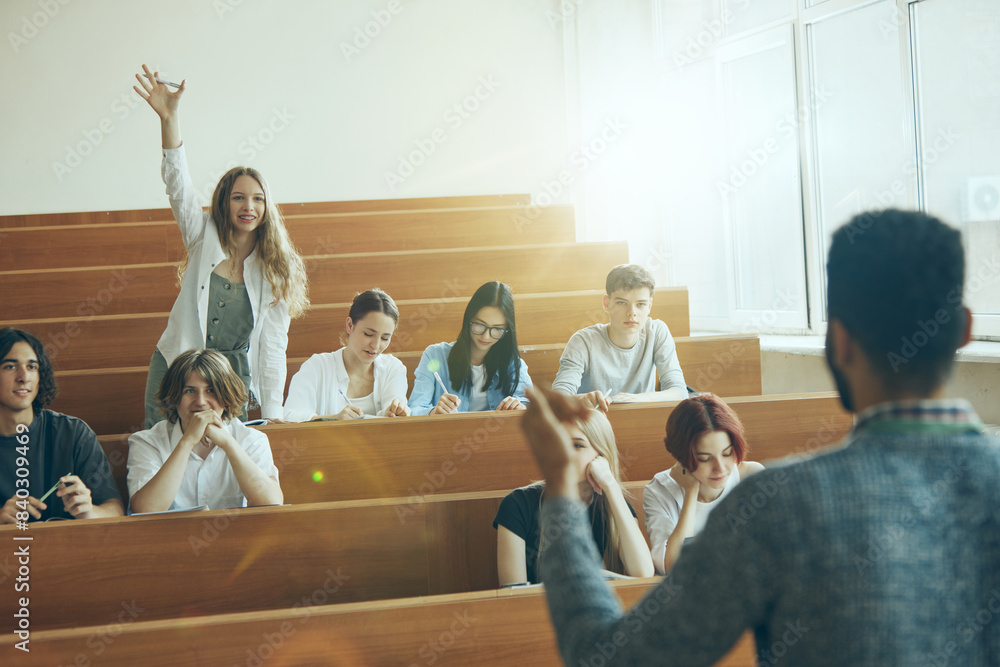 Young girl raising hand to give answer to the teacher during lesson ...