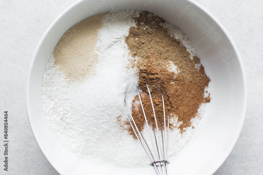 Overhead view of ingredients for making hot cross buns in a white bowl ...