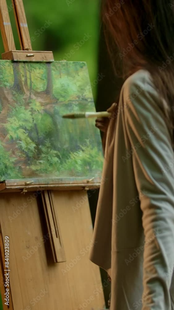 Rear view of a young artist woman painting a landscape in a summer park ...